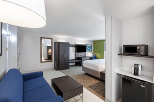 Quarto de hotel moderno com sofá azul, uma pequena mesa de escritório, cama, TV, micro-ondas e mini-geladeira.