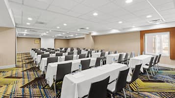Sala de conferências com várias mesas e cadeiras, uma tela de projetor e um carpete estampado.