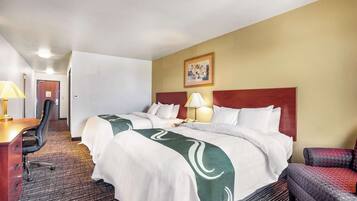 Quarto de hotel com uma cama grande, uma escrivaninha com cadeira, um abajur e um quadro na parede.