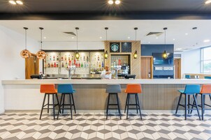 Uma área de bar com balcão, banquetas e diversas garrafas.