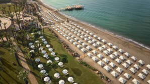 Vista aérea de um resort à beira-mar, com fileiras de guarda-sóis e palmeiras, um píer que se estende para a água, e um edifício com a inscrição 'MARINE RESORT'.