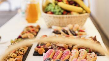Uma mesa de buffet com diversos doces, uma cesta de frutas e um jarro de suco.