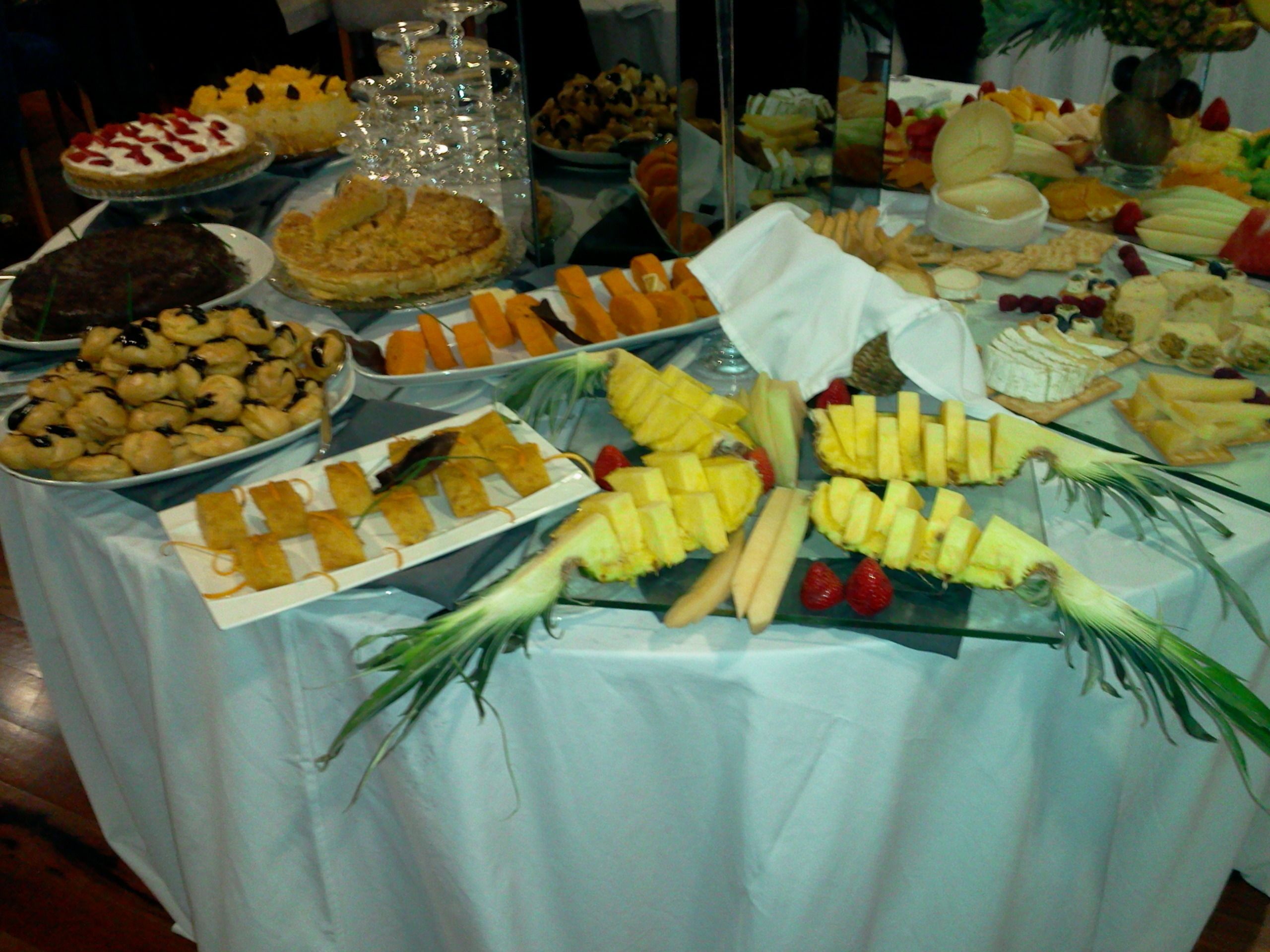 Uma mesa de buffet com diversos alimentos, incluindo bolos, doces, frutas e legumes.