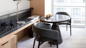 Cozinha moderna com bancada de mármore, armário de madeira, mesa de jantar redonda com duas cadeiras e uma janela grande com vista para a cidade.