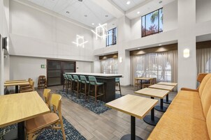 Um saguão de hotel com várias áreas de estar, um bar e uma escadaria que leva a um andar superior.