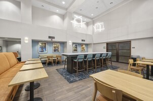 Um espaço amplo e interno com diversas opções de assentos, incluindo mesas e cadeiras, e um bar central.