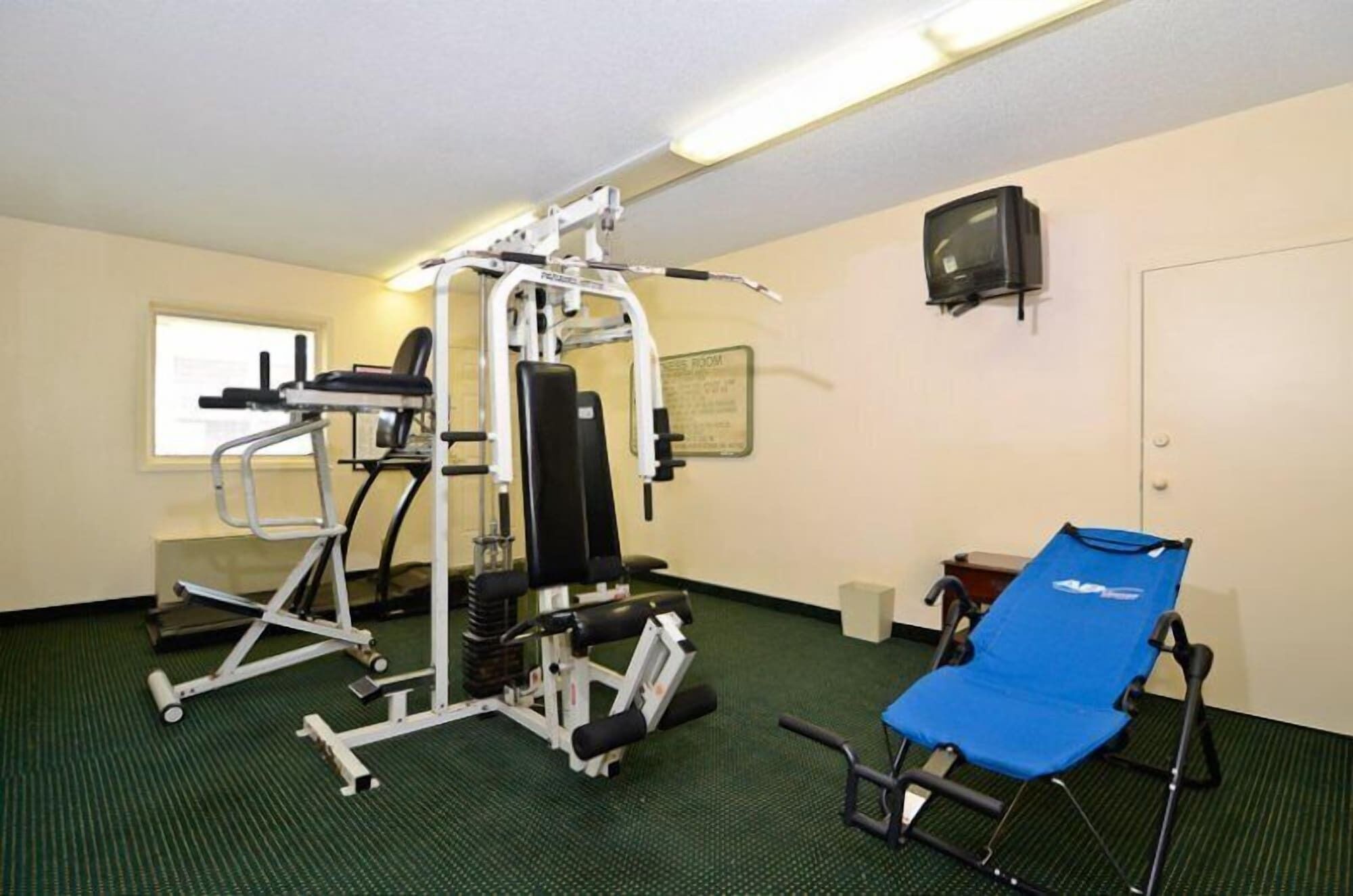 Uma academia com equipamentos de exercícios, uma mesa de massagem azul e uma televisão na parede.