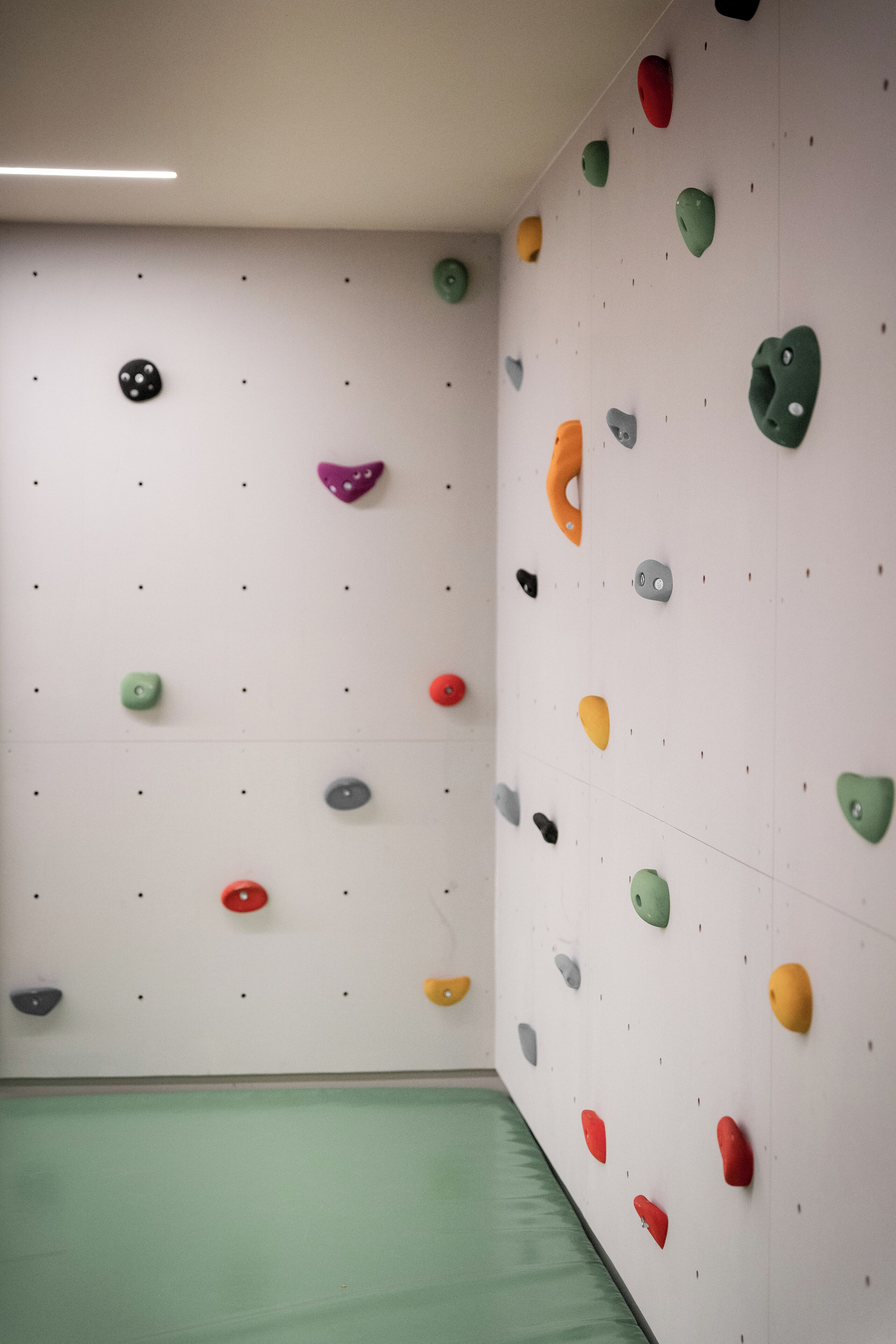 Uma parede de escalada com pontos de apoio de várias cores e um chão acolchoado.