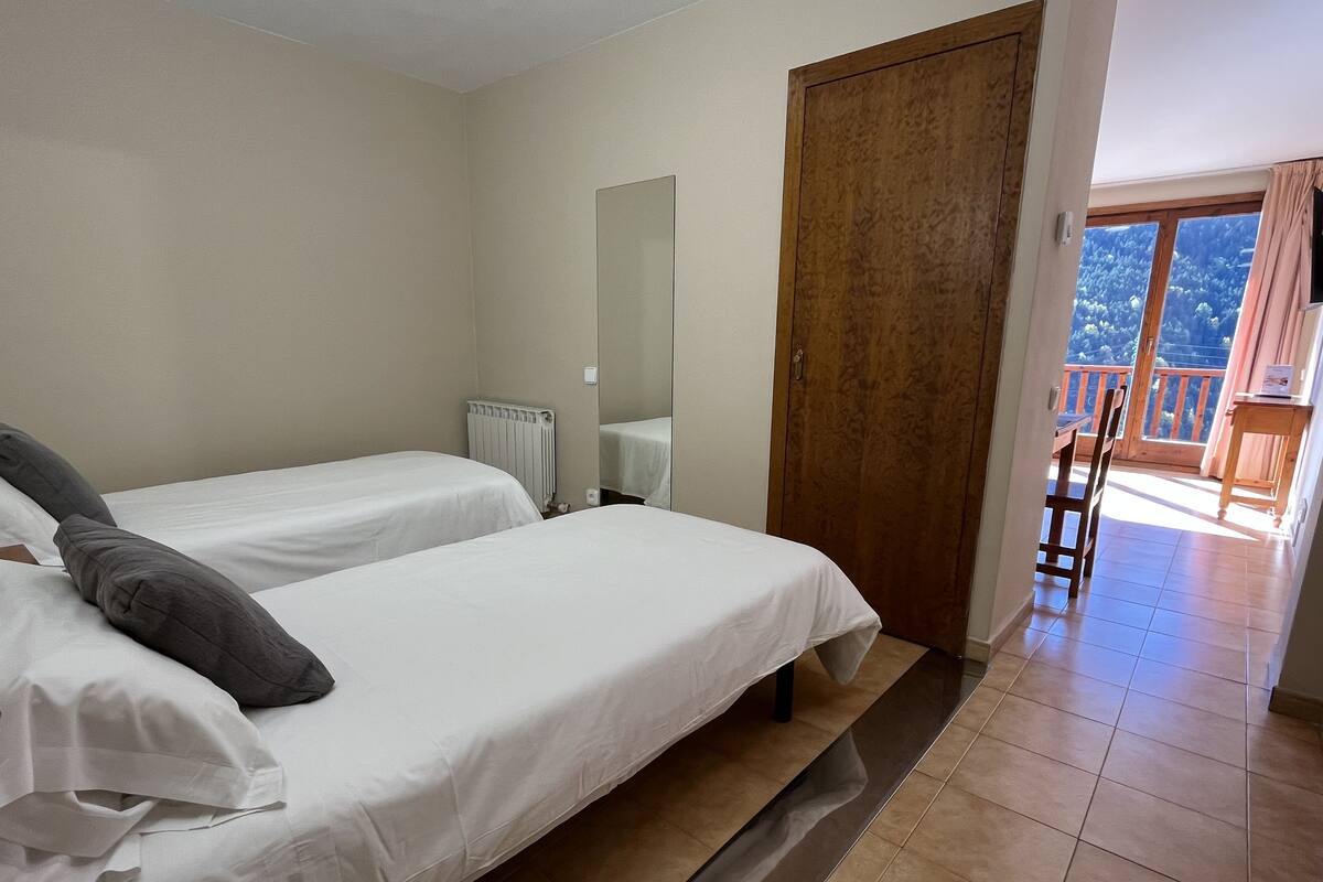 Quarto com duas camas, um radiador, uma porta de madeira e uma varanda com vista.