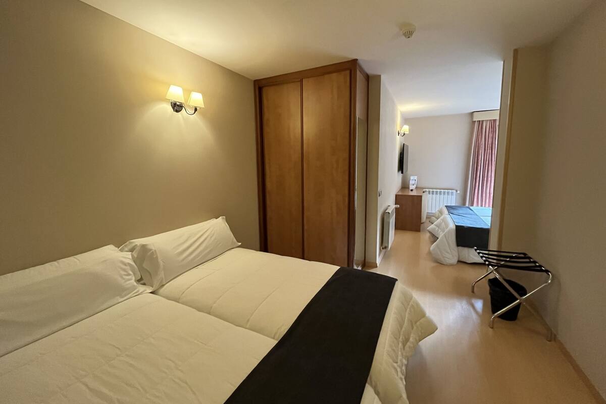 Quarto de hotel com uma cama grande, um guarda-roupa de madeira, uma kitchenette pequena e uma casa de banho com chuveiro.