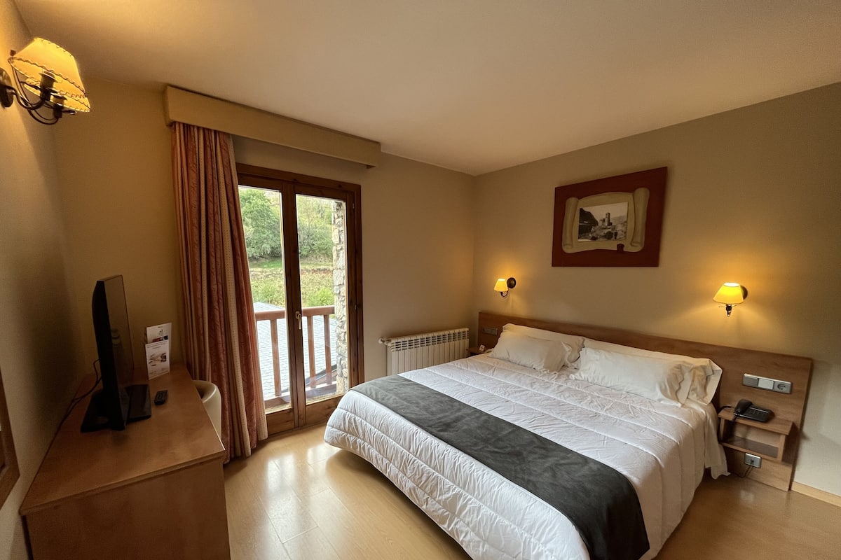 Quarto de hotel com cama, escrivaninha com computador, telefone e duas luminárias de parede.