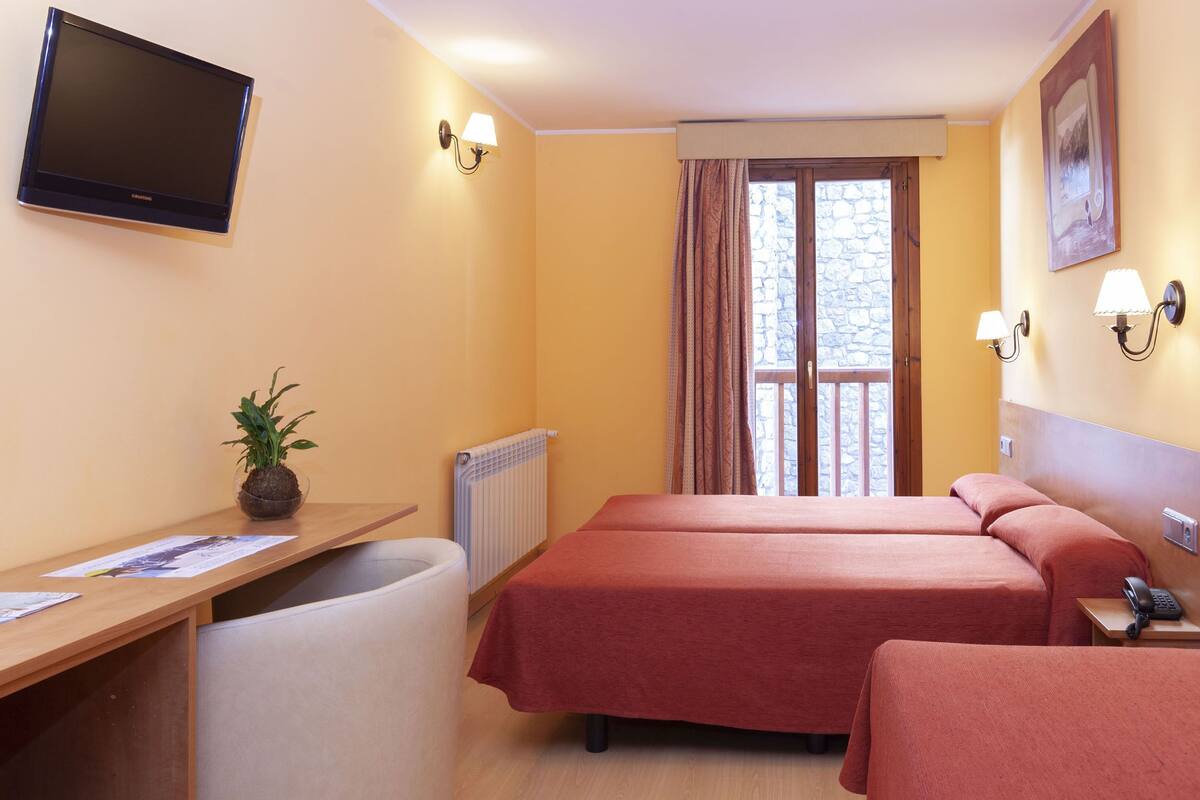 Quarto de hotel com duas camas, uma escrivaninha, uma cadeira, uma televisão e uma janela com cortinas.