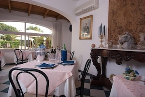 Uma sala de jantar com uma mesa posta para quatro pessoas, rodeada por cadeiras, um aparador decorativo e uma janela com cortinas.