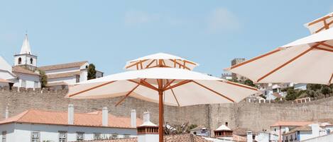 Terraço com espreguiçadeiras e guarda-sóis, com vista para um centro histórico com edifícios e uma igreja.
