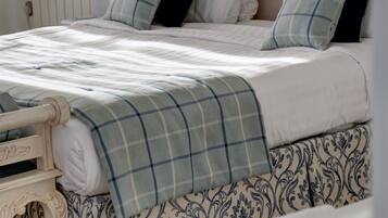 Uma cama bem arrumada com um edredom quadriculado branco e azul, uma saia azul e branca estampada combinando, e uma cabeceira branca com entalhes elaborados.