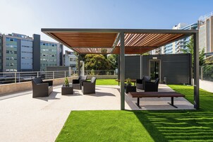 Um pátio externo com assentos, uma pérgula e vista para edifícios ao redor.