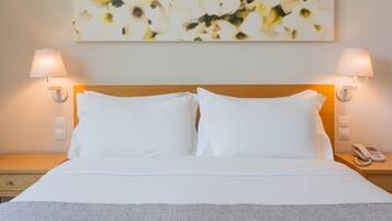Quarto de hotel com uma cama grande, duas luminárias de cabeceira, um telefone e uma obra de arte na parede.