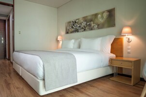 Quarto de hotel moderno com cama grande, abajures, mesa de cabeceira e um quadro na parede.