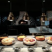 Uma cozinha comercial com forno de tijolos, diversas estações de preparação de alimentos e luminárias pendentes.