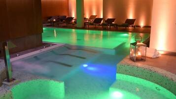 Piscina interior com iluminação verde, espreguiçadeiras e piso revestido de azulejos.