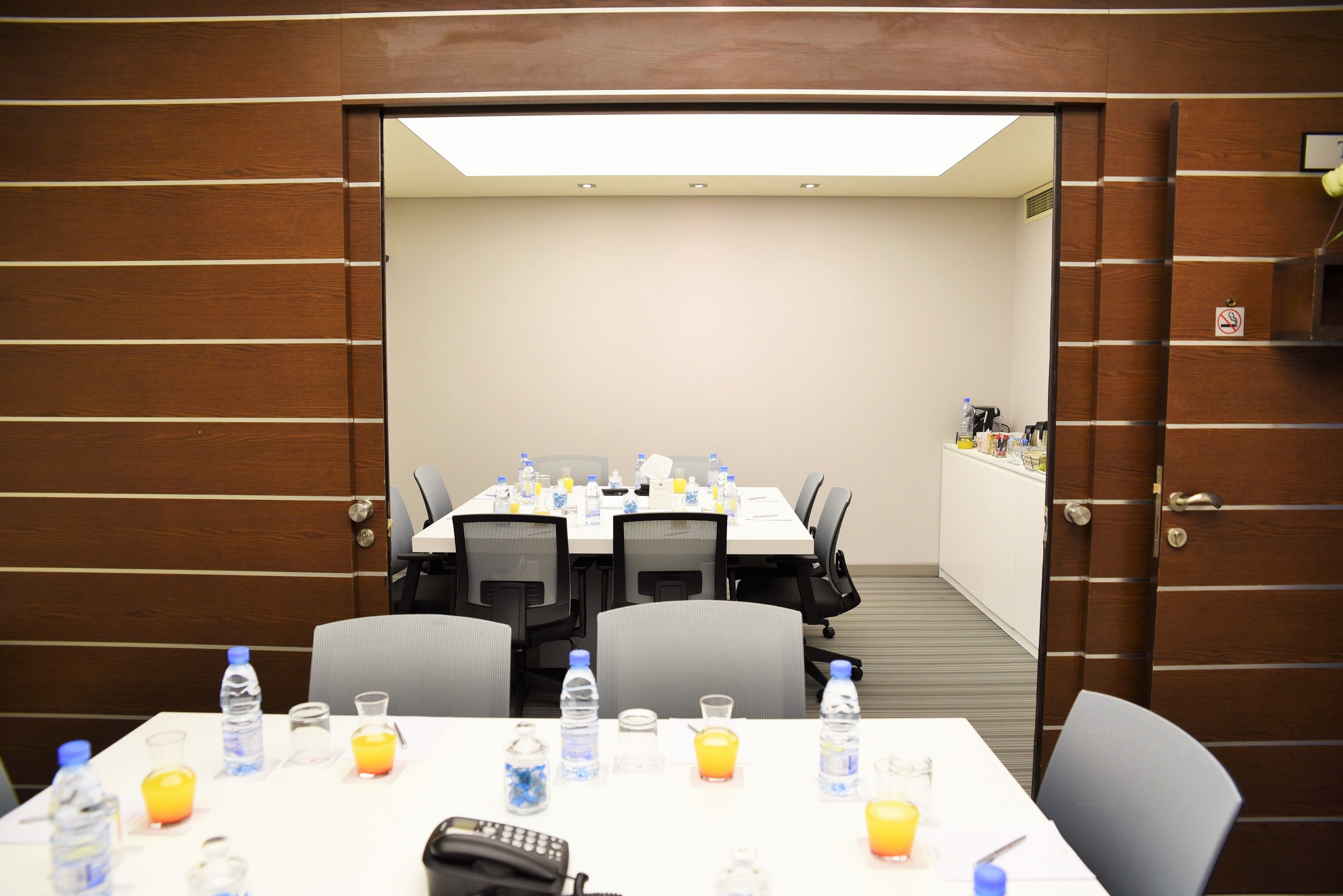 Sala de conferência com mesa preparada para uma reunião, equipada com garrafas de água, copos e um telefone.