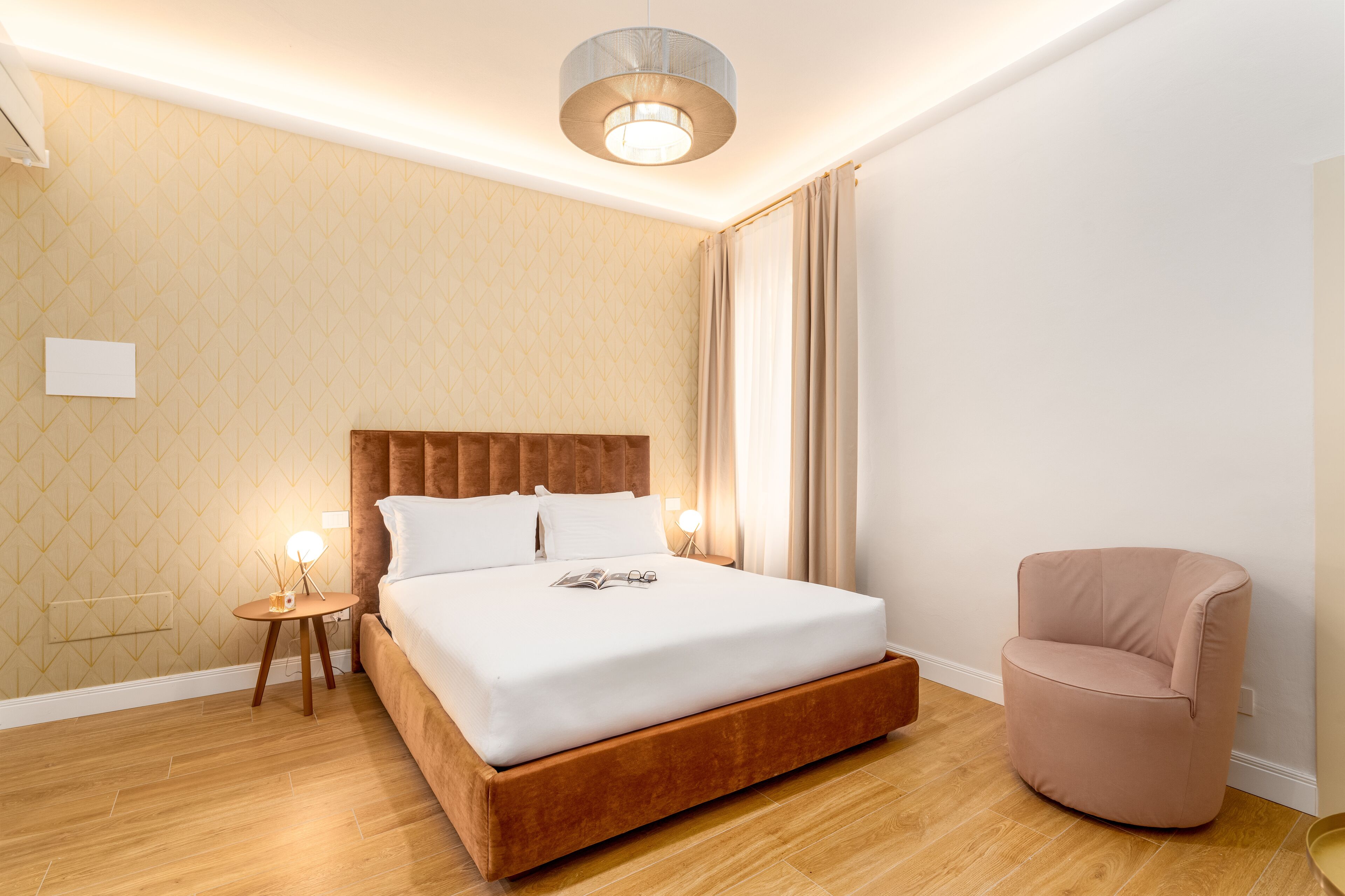 Quarto de hotel com uma cama grande, mesas de cabeceira, uma cadeira e um lustre.