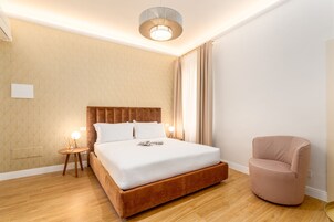 Quarto de hotel com uma cama grande, mesas de cabeceira, uma cadeira e um lustre.