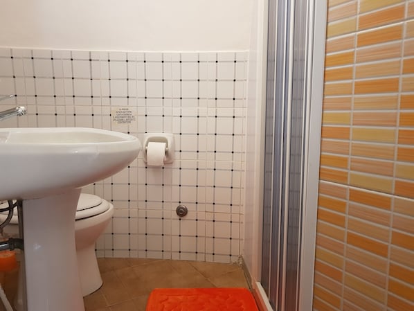 Casa de banho com lavatório branco, sanita e zona de duche com porta de vidro.