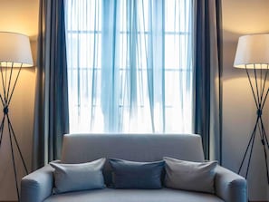 Uma sala de estar moderna com um sofá, duas luminárias de chão e cortinas translúcidas.