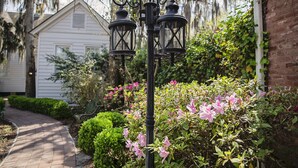 Um jardim com um caminho, uma casa branca e um poste de luz preto.