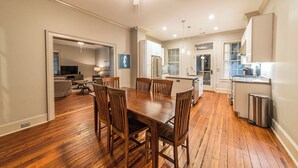 Uma sala de estar ampla com uma mesa de jantar e cadeiras de madeira, uma cozinha com armários brancos e uma janela grande.
