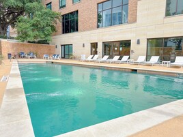 Piscina com cadeiras de descanso e um edifício de tijolos ao fundo.