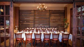 Restaurante com parede de adega de vinhos, mesas e cadeiras de madeira.