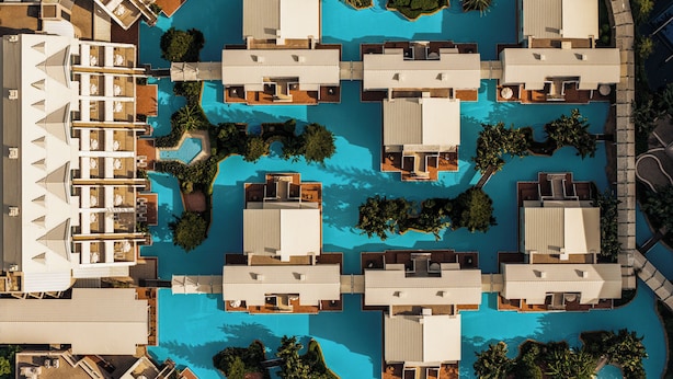 Resort com várias bangalôs sobre a água dispostos em torno de uma piscina central, interligados por passarelas.
