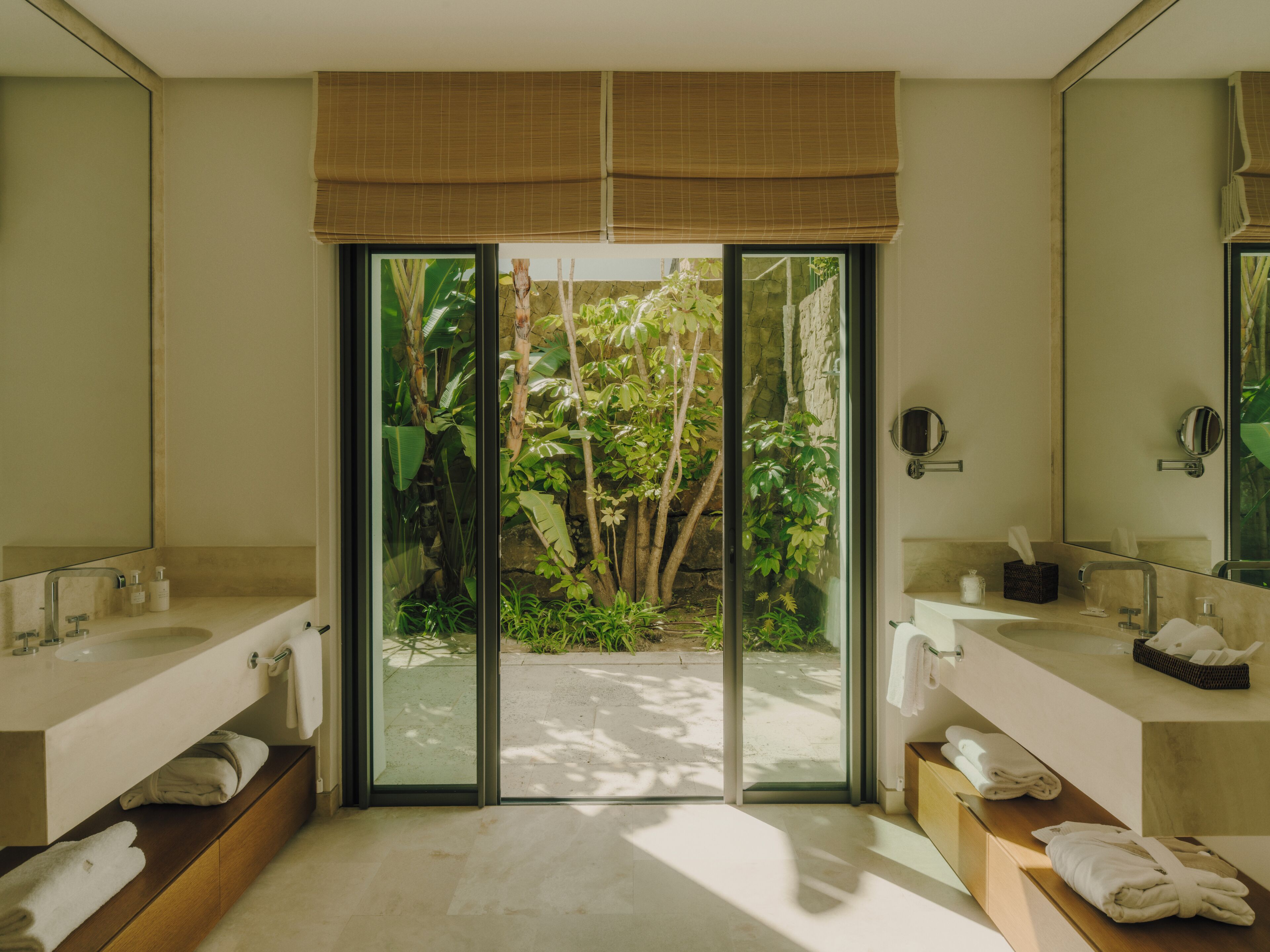 Um banheiro moderno com duas pias, um espelho grande e uma porta de vidro deslizante para um jardim.