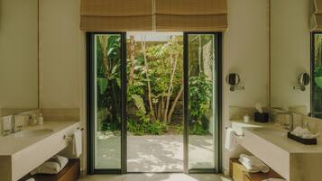 Um banheiro moderno com duas pias, um espelho grande e uma porta de vidro deslizante para um jardim.
