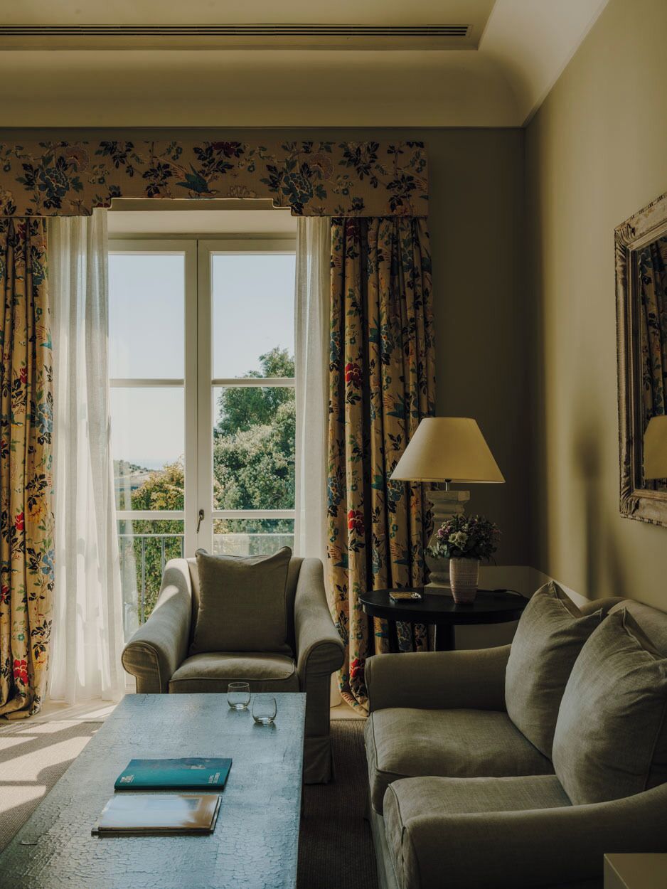 Um quarto com sofá, mesa de centro, abajur e janela com cortinas.