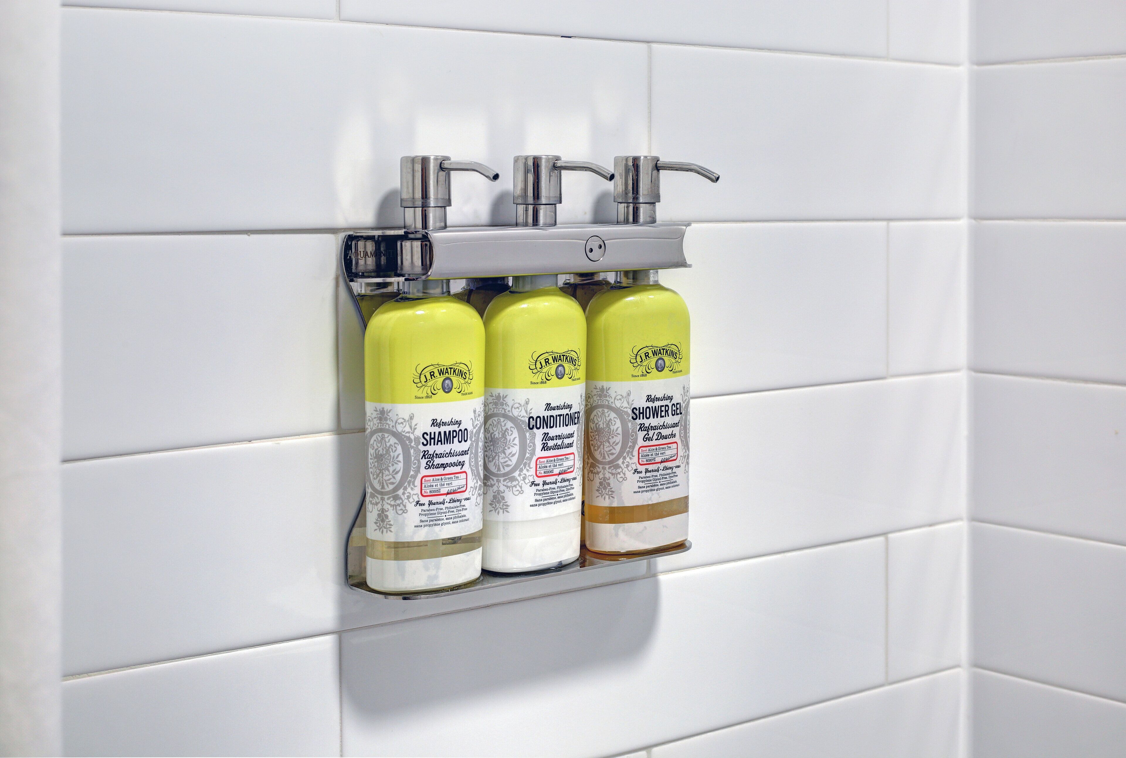 Um dosador fixado na parede com três frascos de shampoo e gel de banho J.R. Watkins.