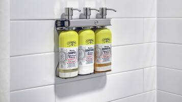 Um dosador fixado na parede com três frascos de shampoo e gel de banho J.R. Watkins.
