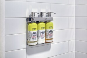 Um dosador fixado na parede com três frascos de shampoo e gel de banho J.R. Watkins.