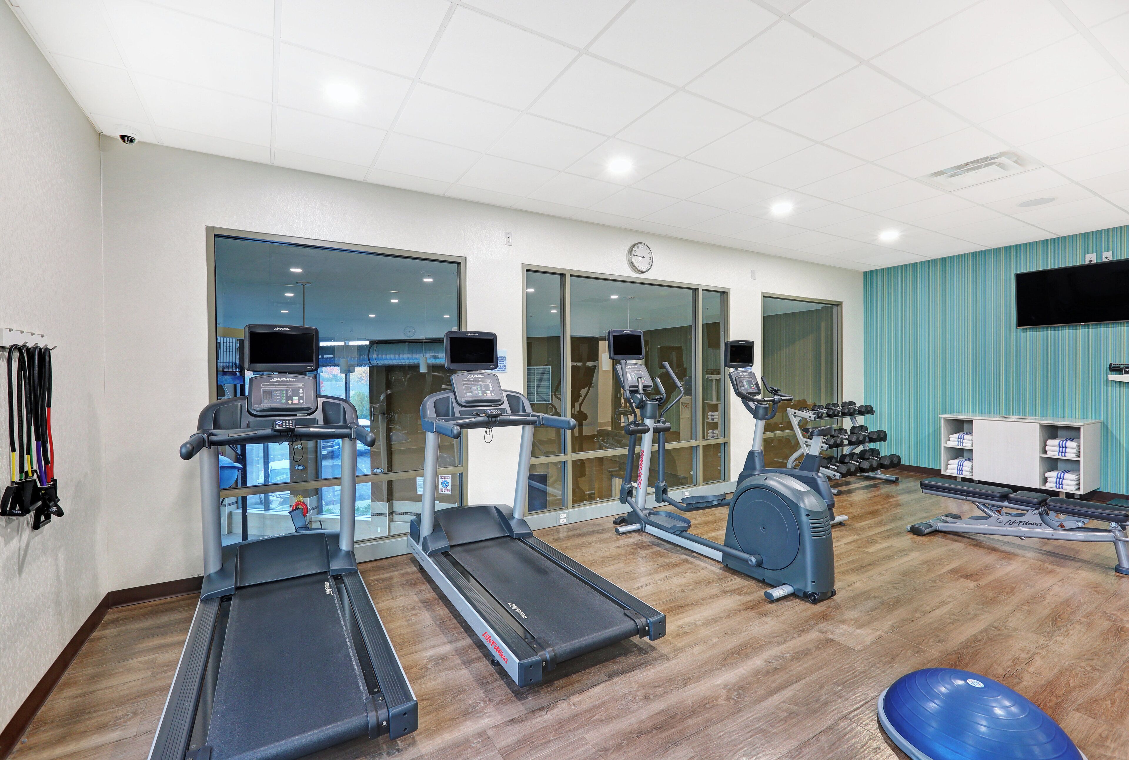 Academia com esteiras, elípticos e um banco de musculação.