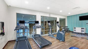 Academia com esteiras, elípticos e um banco de musculação.