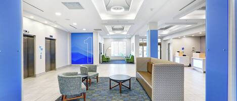 Um hall moderno com balcão de recepção, área de estar, elevadores e um tapete estampado.