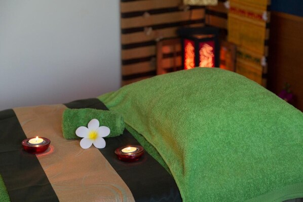 Uma cama de spa com toalhas verdes, uma flor branca e duas velas acesas.