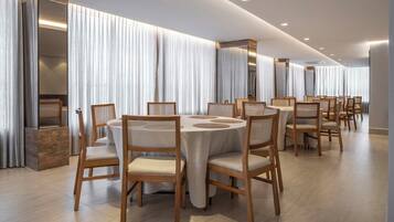 Uma sala de jantar moderna com mesas redondas, cadeiras de madeira e uma janela grande com cortinas.