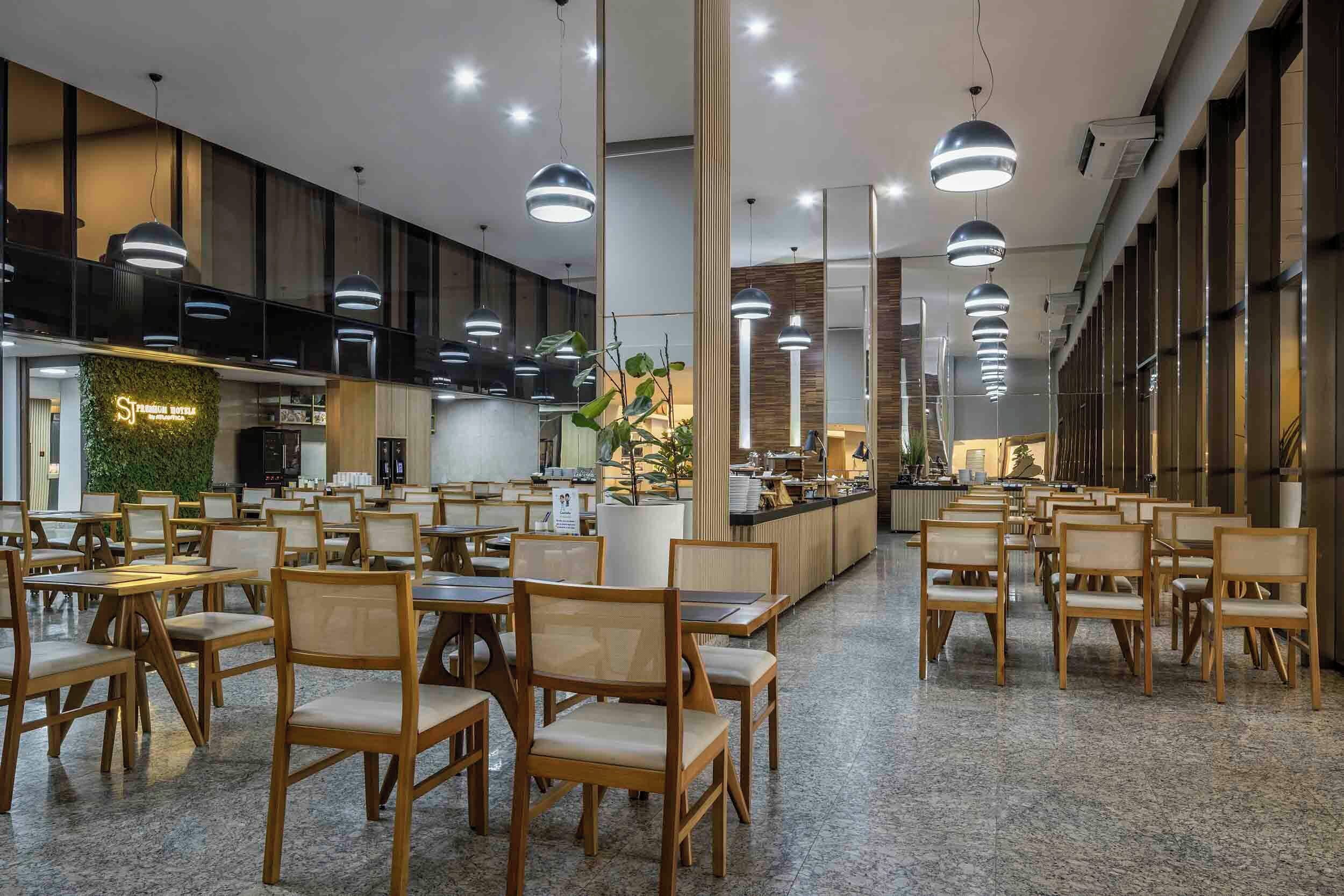 Uma ampla área de refeições interna, com várias mesas e cadeiras, um balcão central com cardápio e iluminação pendente.