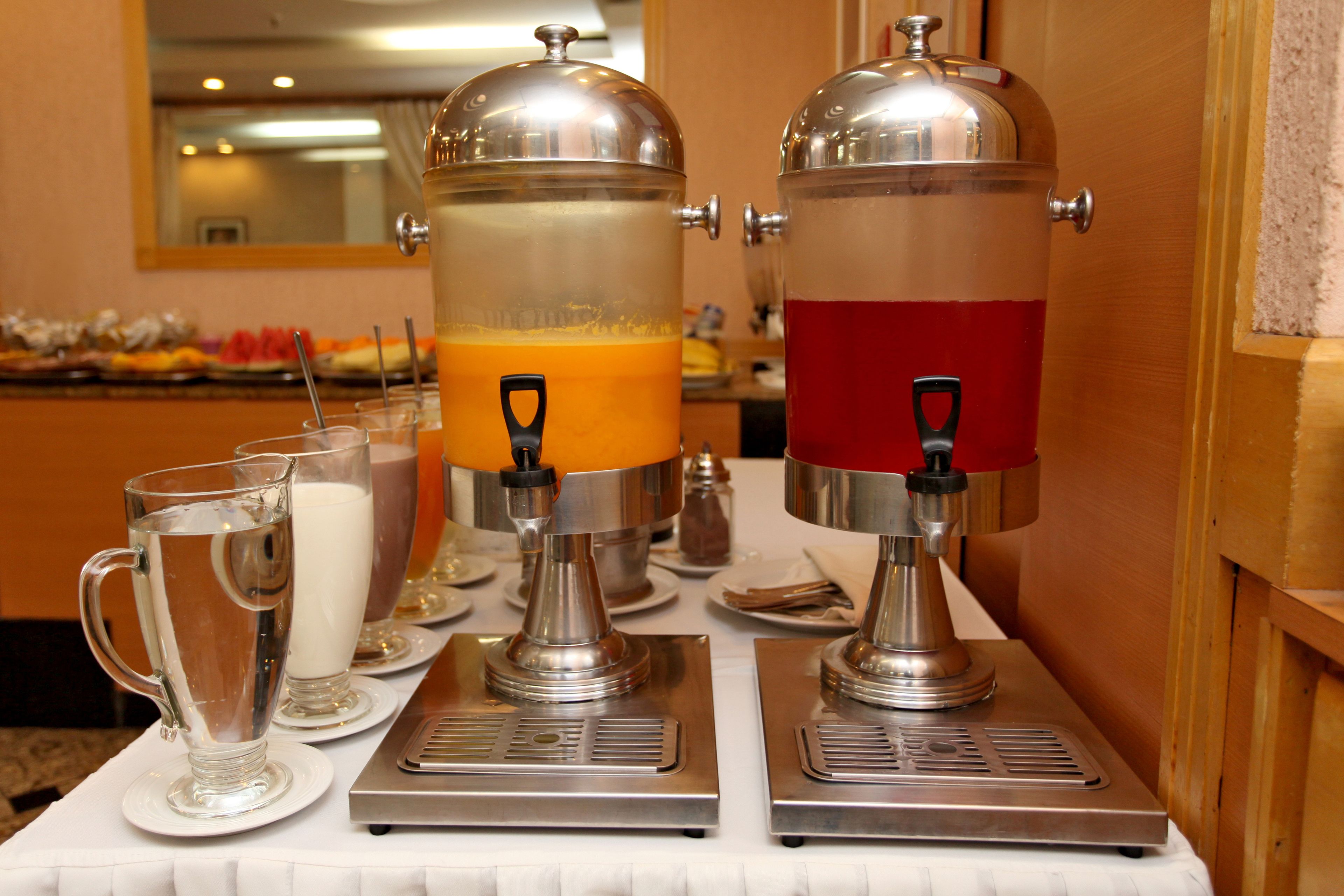 Buffet de café da manhã com dois dispensadores de bebidas, um jarro de leite e um copo de suco de laranja.