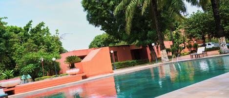 Piscina com deck ladrilhado, rodeada por palmeiras e vegetação.