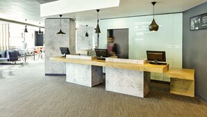 Uma receção com design moderno, destacando-se uma base de betão e um tampo de madeira. Três pendentes iluminam a área da receção.
