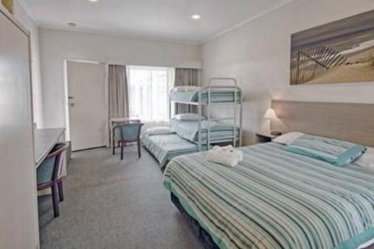 Quarto de hotel com beliches, escrivaninha e uma cadeira.